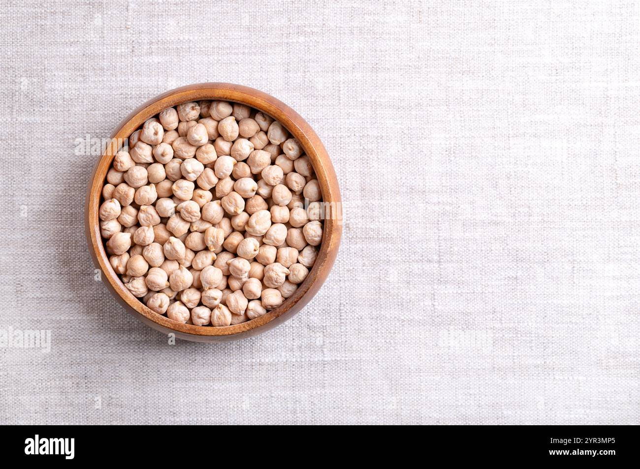 Dried chickpeas in a wooden bowl, on linen fabric, with empty space for ...