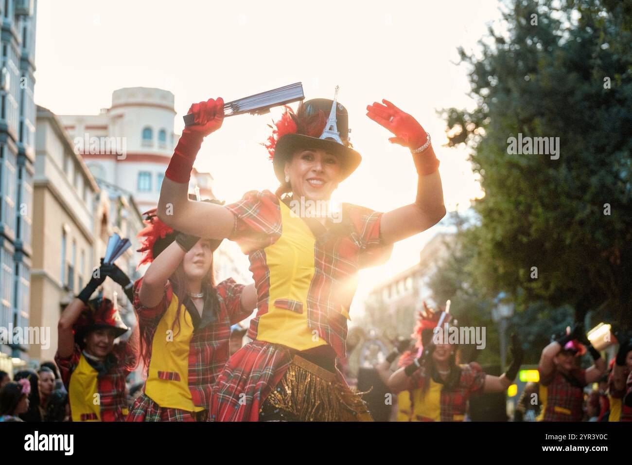 The image depicts a lively street scene with a group of people dressed ...