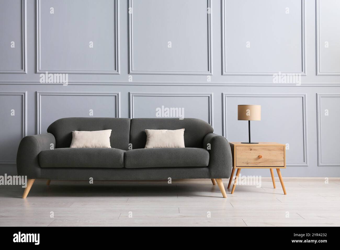 Stylish sofa with cushions and lamp on side table near grey wall Stock ...