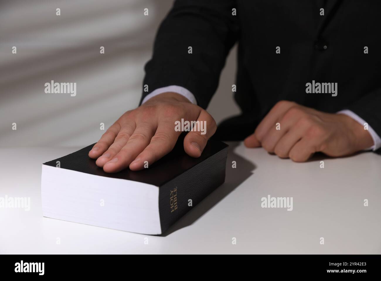 Man taking oath with his hand on Bible at white table, closeup Stock ...