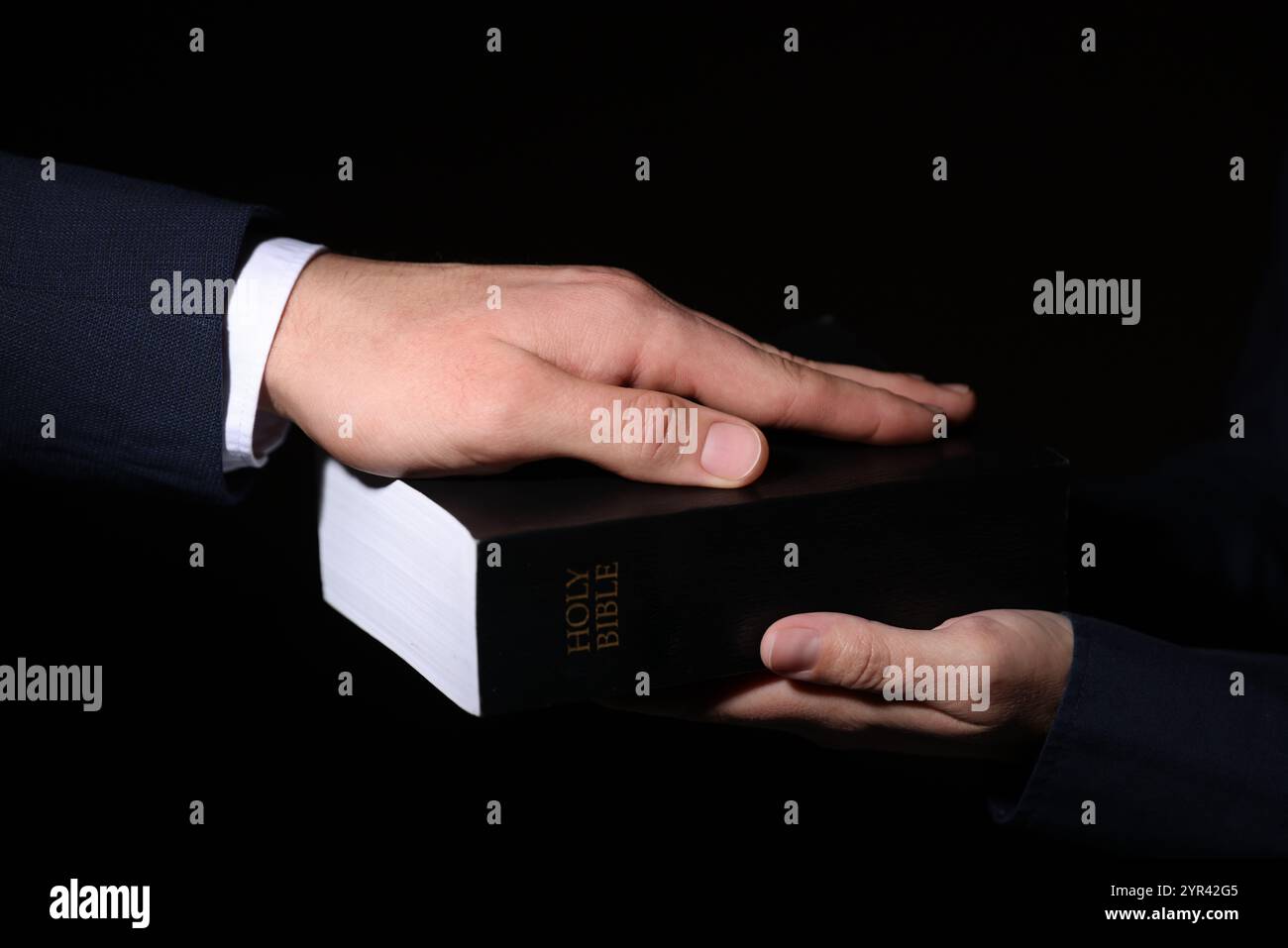 Man taking oath with his hand on Bible against black background ...