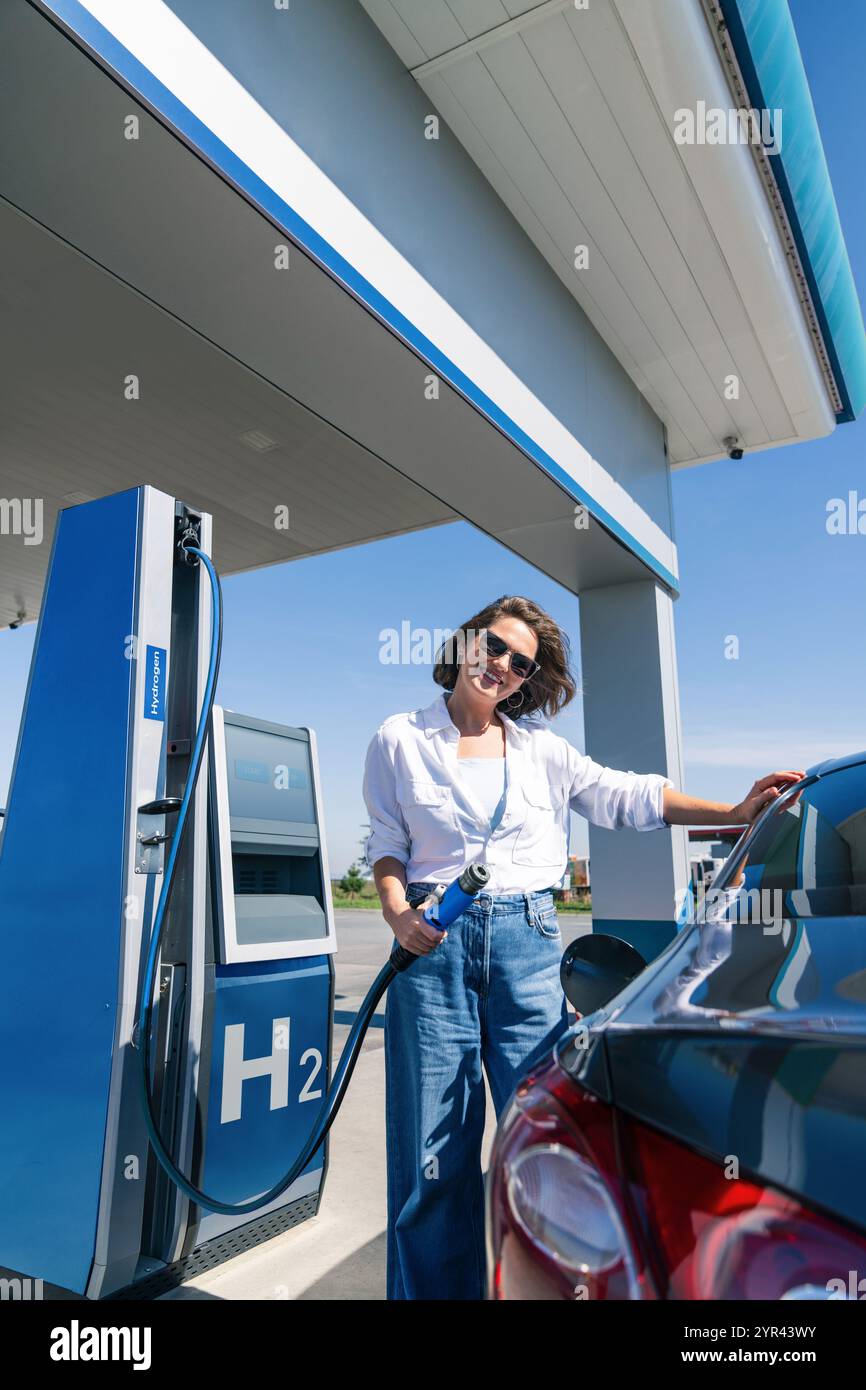 Woman holds a hydrogen fueling nozzle on a hydrogen filling station ...