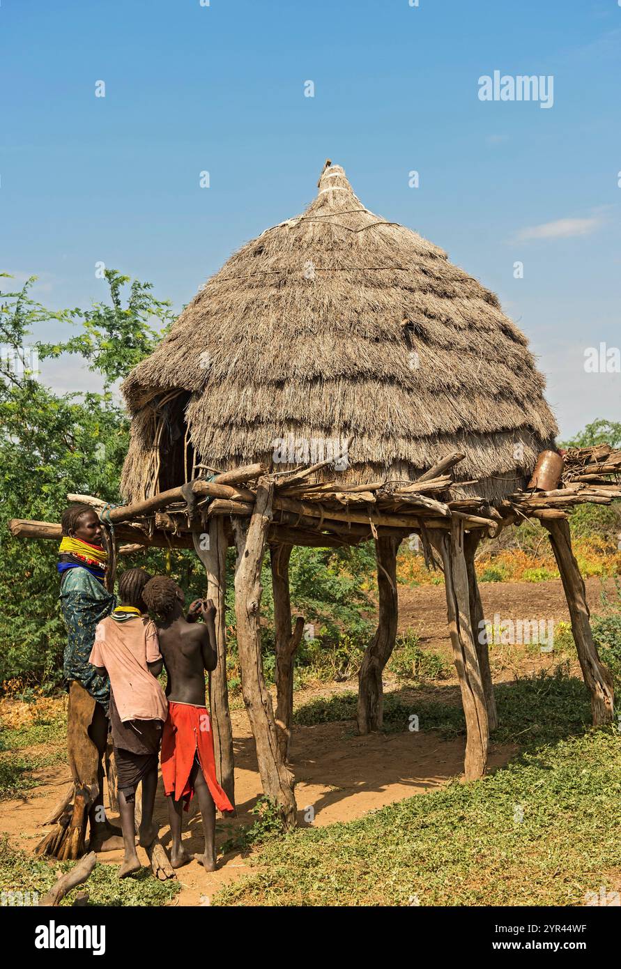 Mother and kids standing at a stilted granary with a thatched roof ...