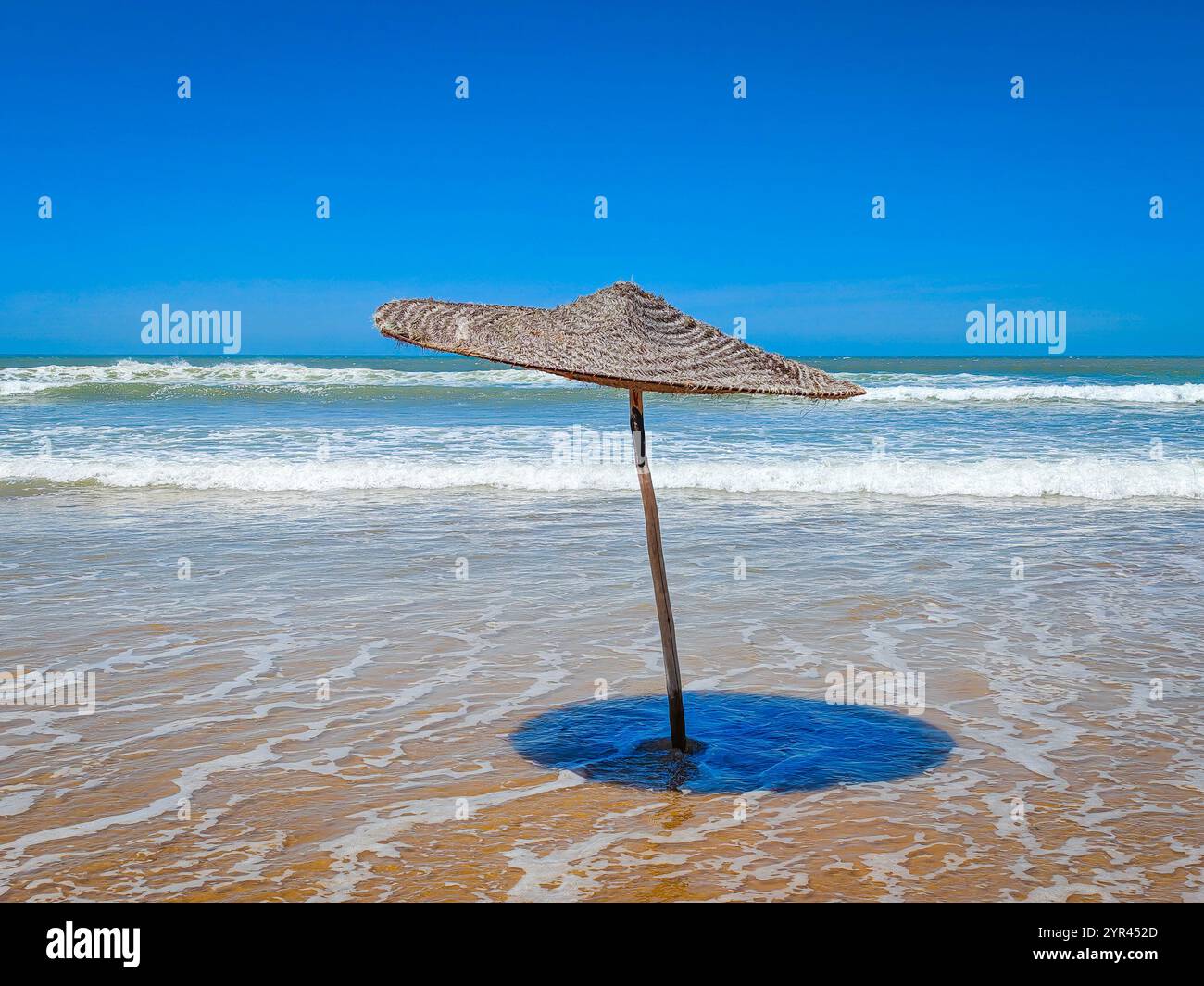 Beach straw umbrella on a deserted beach making a shadow. Parasol ...
