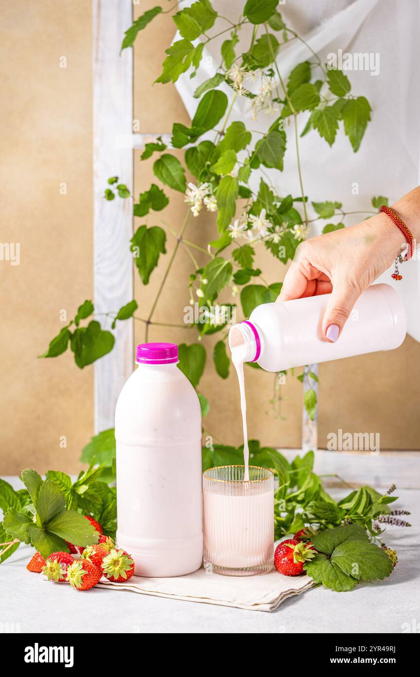 Hand pouring strawberry yogurt from bottle into glass, with fresh ...