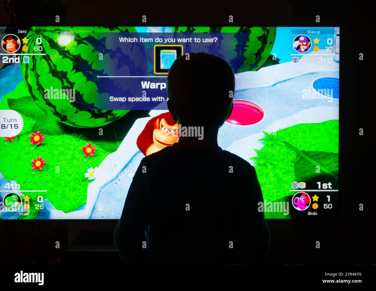 Silhouette of a boy standing in front of a large TV screen watching the ...