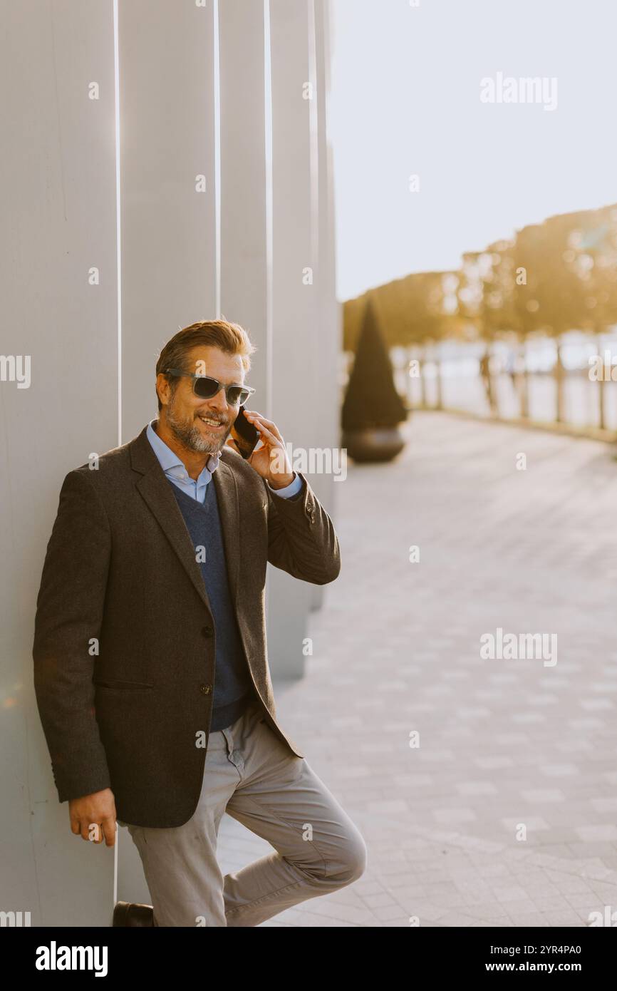 A well-dressed man is leaning casually against a sleek white wall while ...