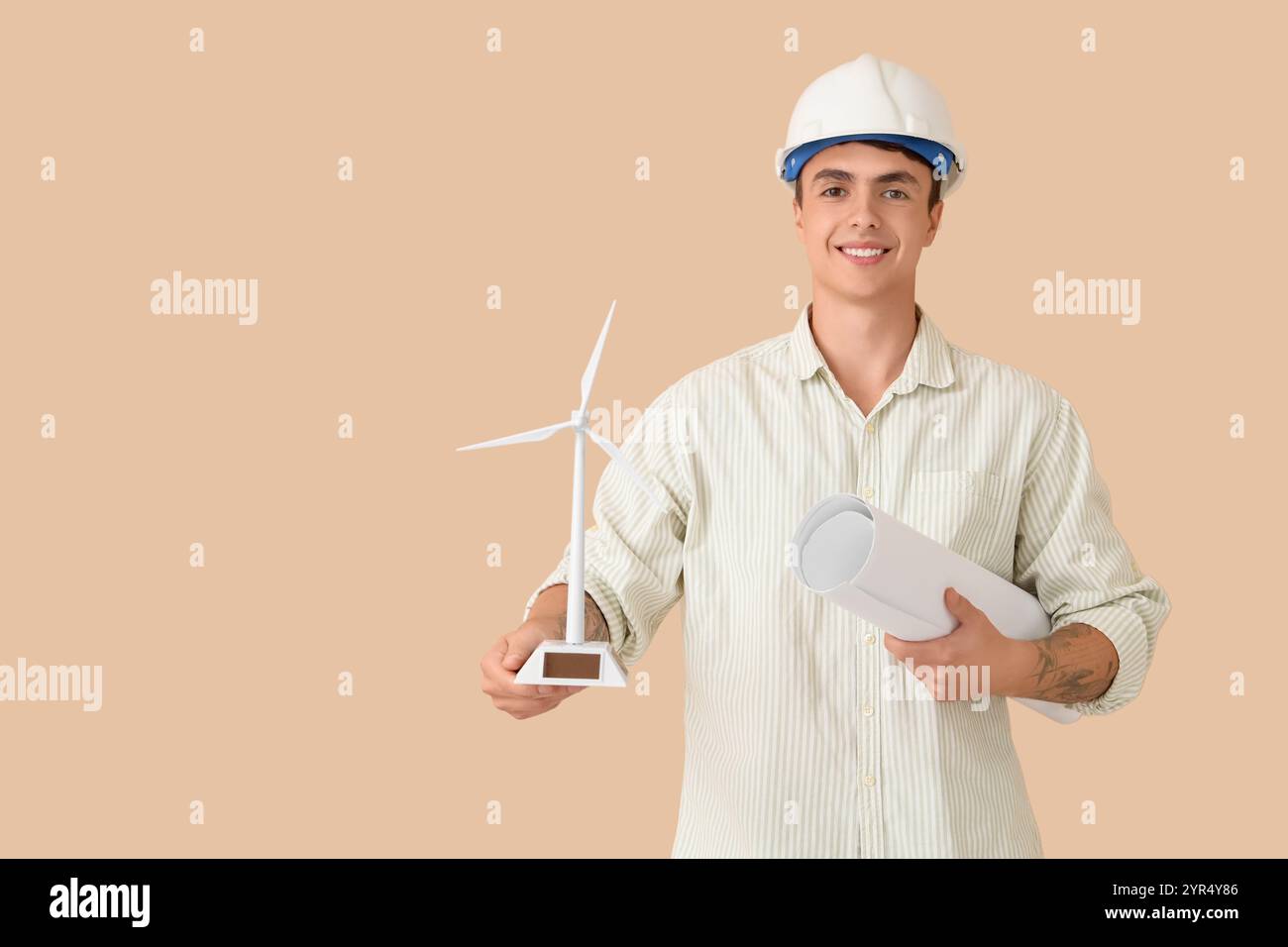 Male engineer with wind turbine model and project on beige background ...