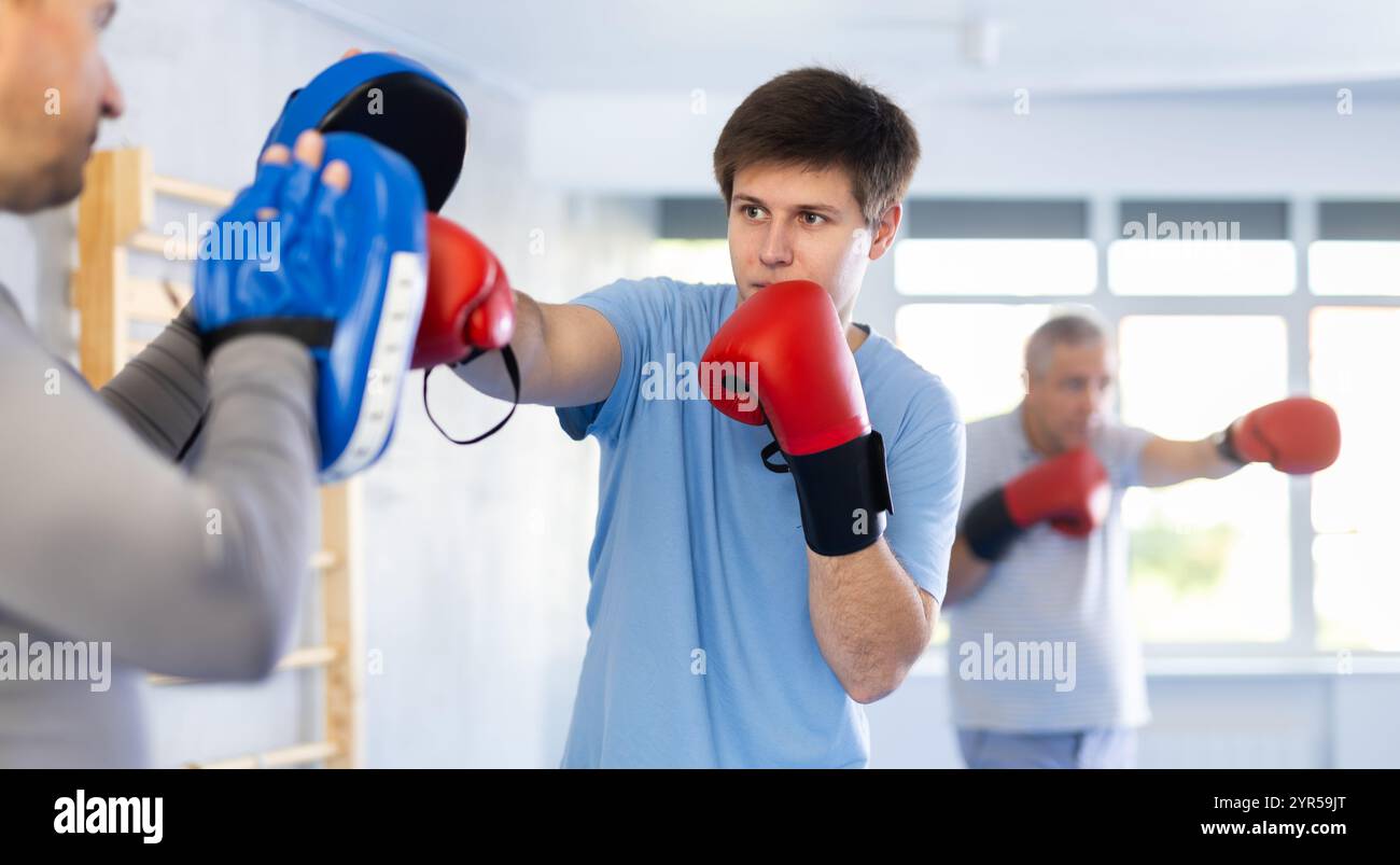 Guy in boxing gloves practicing punches on mitts with coach during self ...