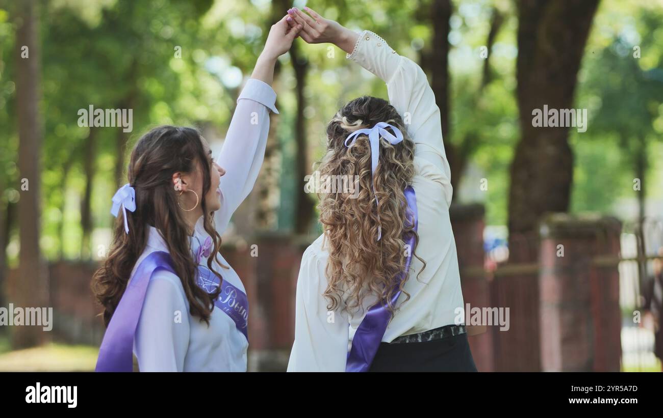 Two students in graduation sashes joyfully dance together in the ...