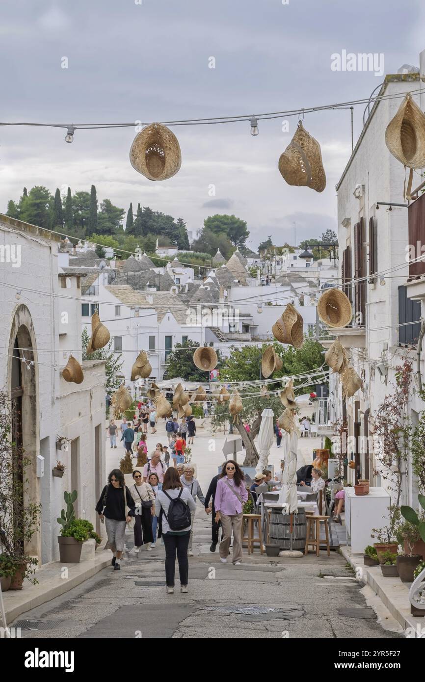 A lively street with hanging straw hats and white buildings, bustling ...