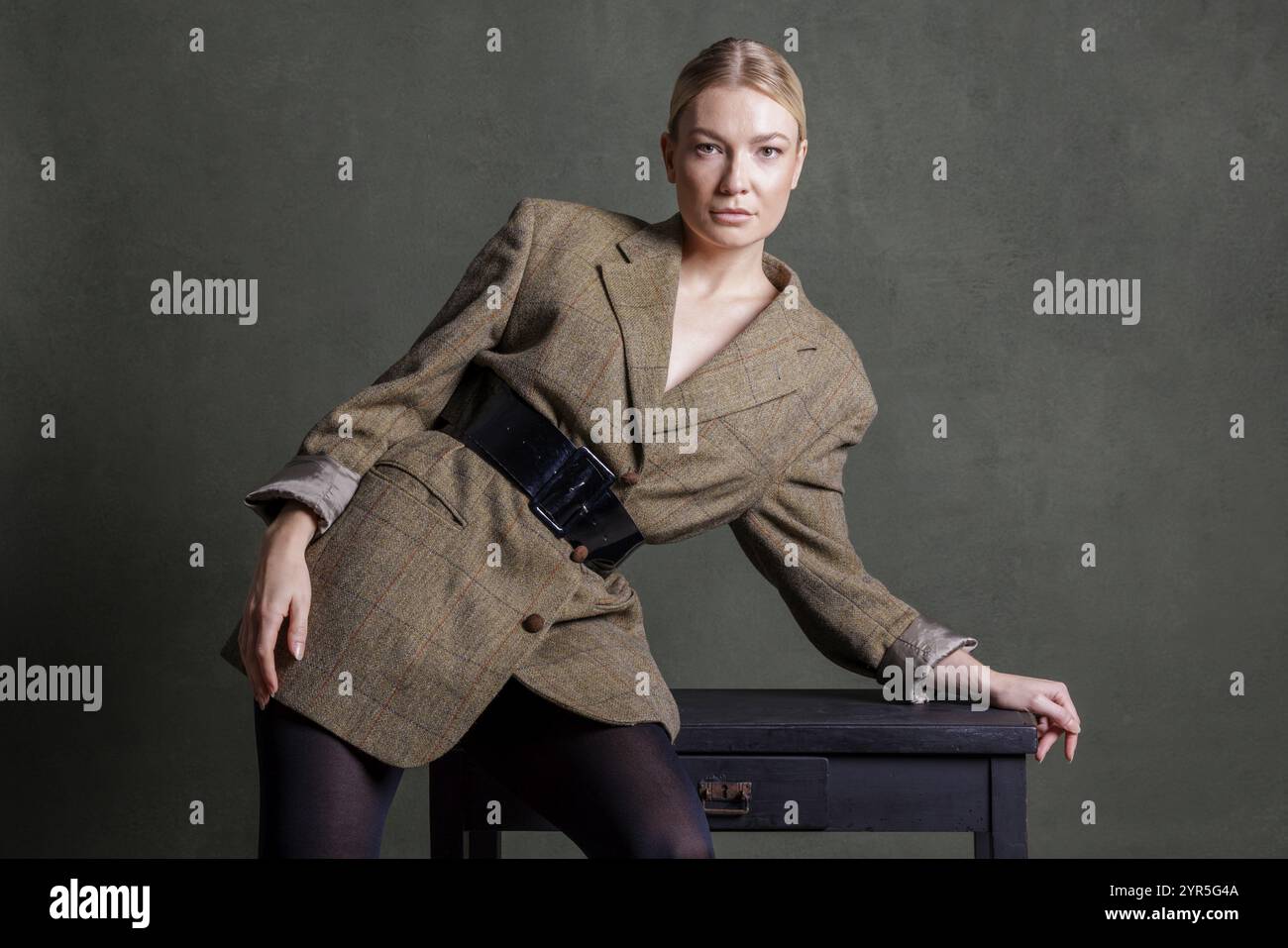 Fashionably dressed woman leaning against a table in front of a green ...