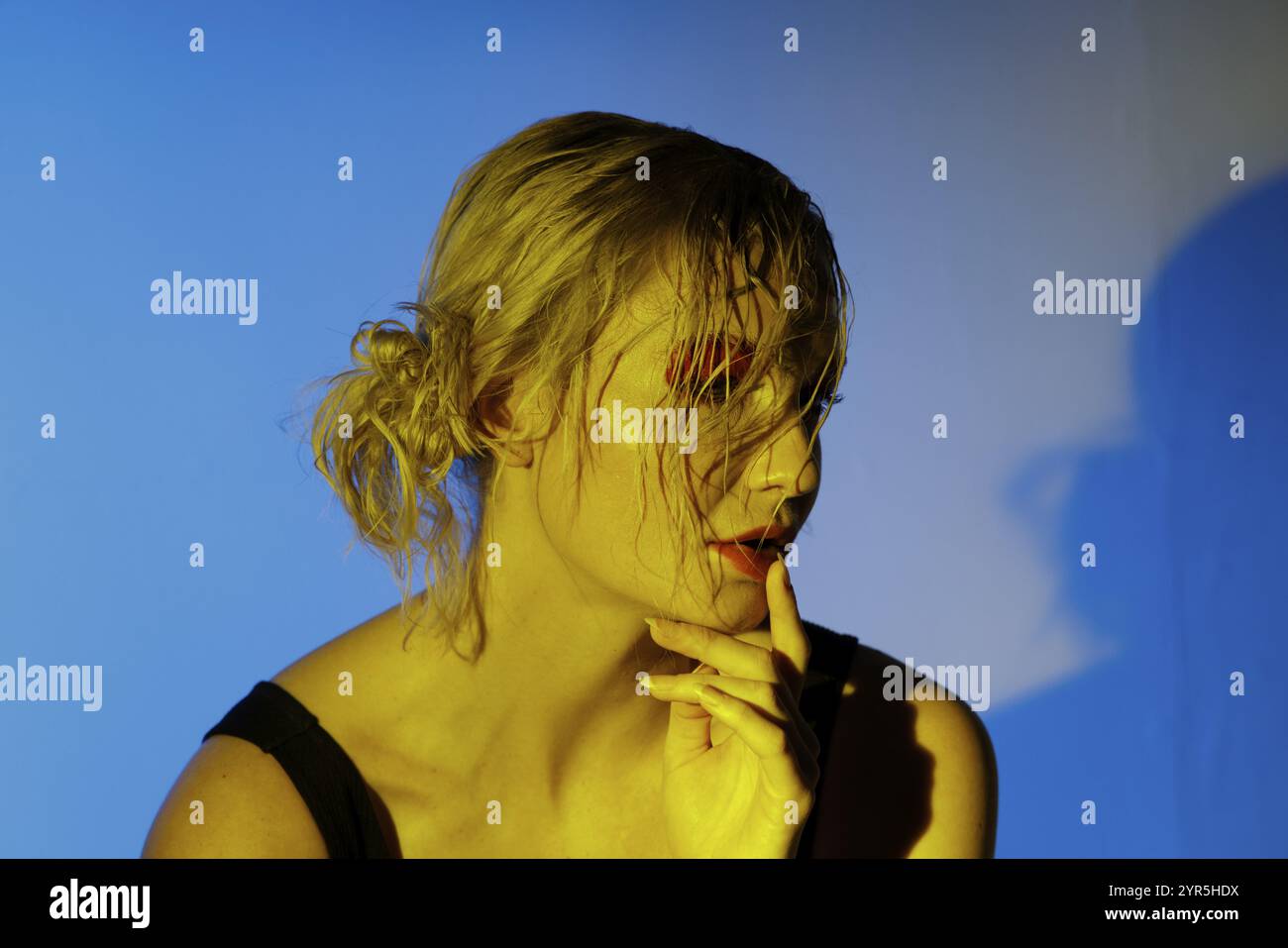 Woman in yellow light with wet hair in front of blue background ...