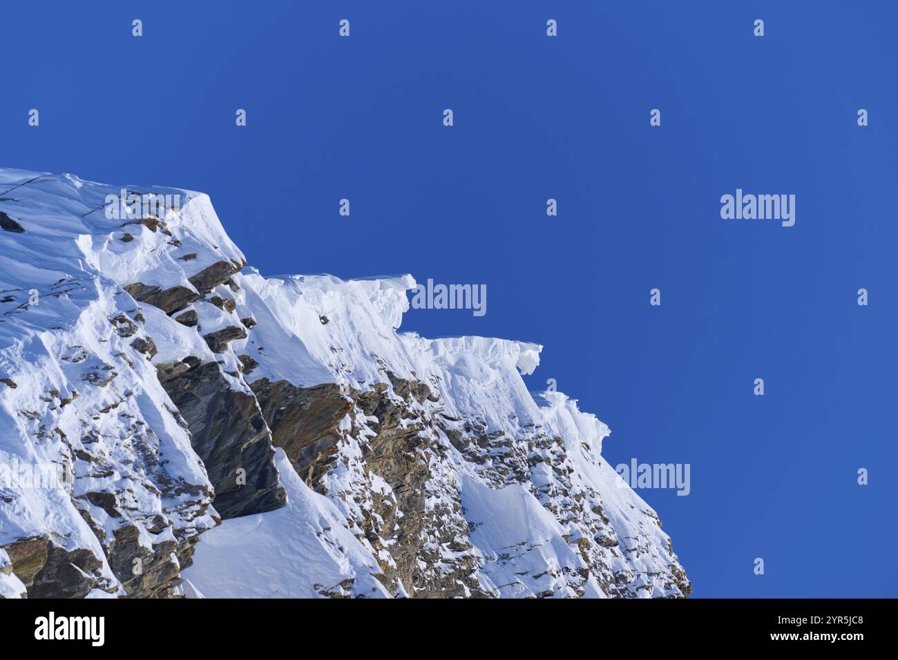 Snow-covered mountain peak with snow cornices under a clear blue sky ...