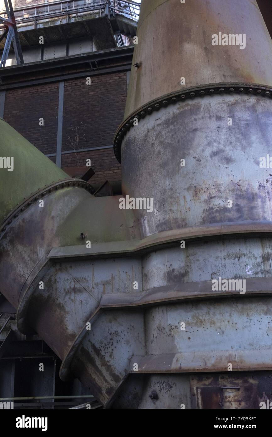 Large, rusted industrial pipes form part of an old factory environment ...