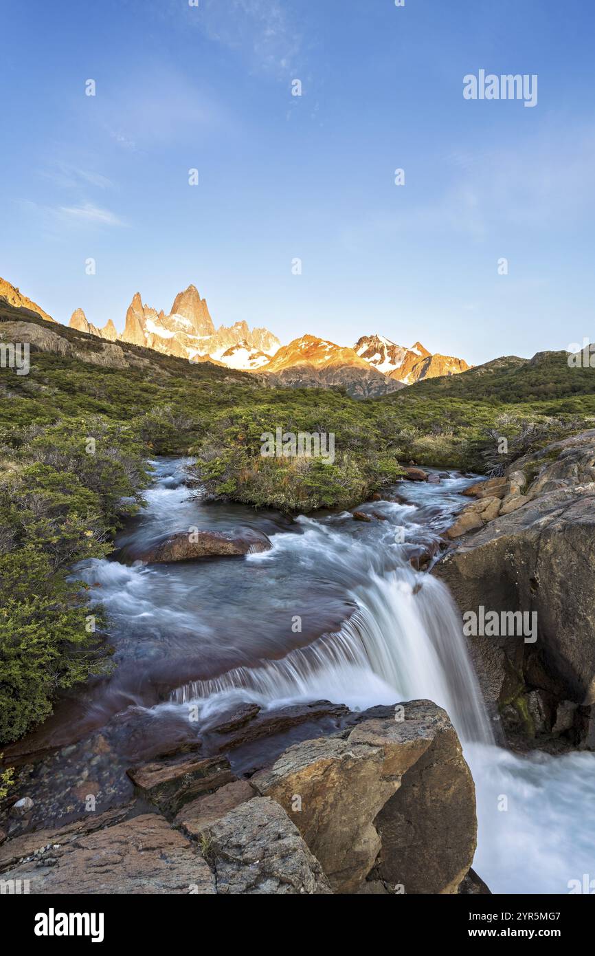 A waterfall with the Fitz Roy mountain illuminated by the morning sun ...