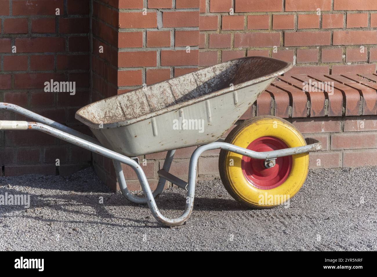 Rustic wheelbarrow with a yellow wheel resting against a brick wall ...