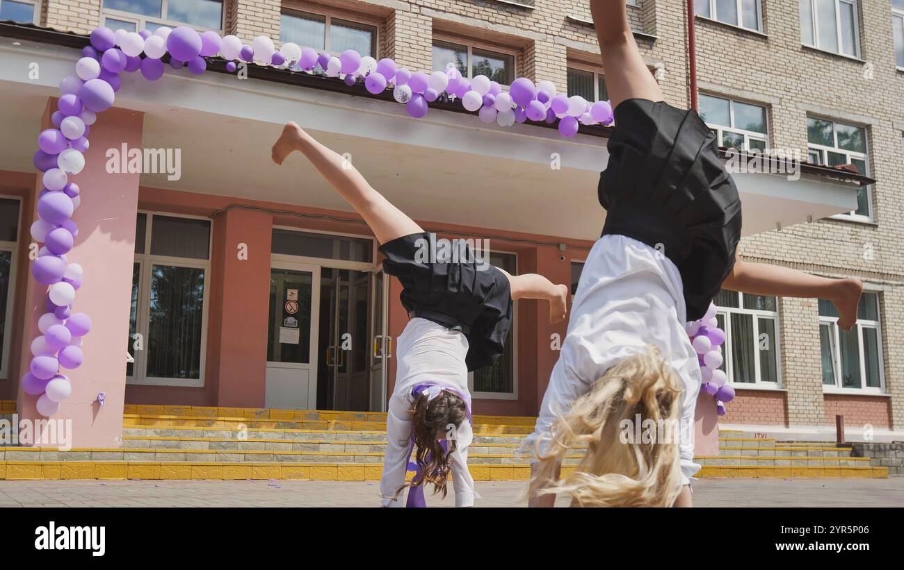 Two schoolgirls doing cartwheels in front of their school on the last ...