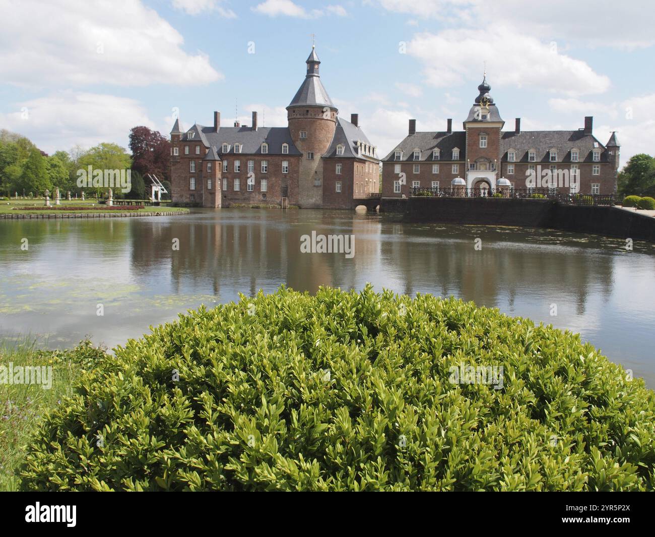 View of a castle behind a large green bush and moat, anholt, westphalia ...
