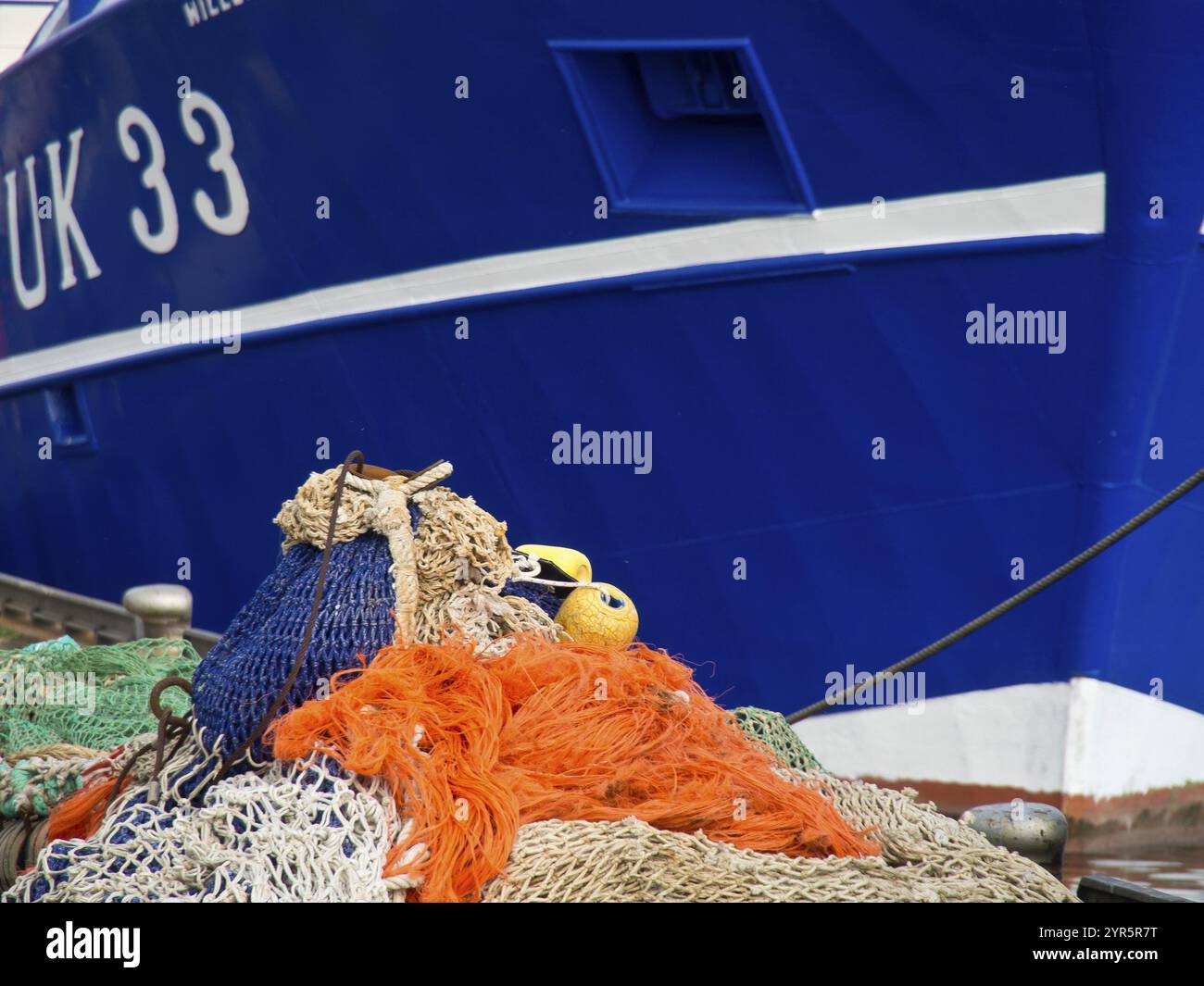 A blue ship in the harbour, in front of it a stack of colourful fishing ...