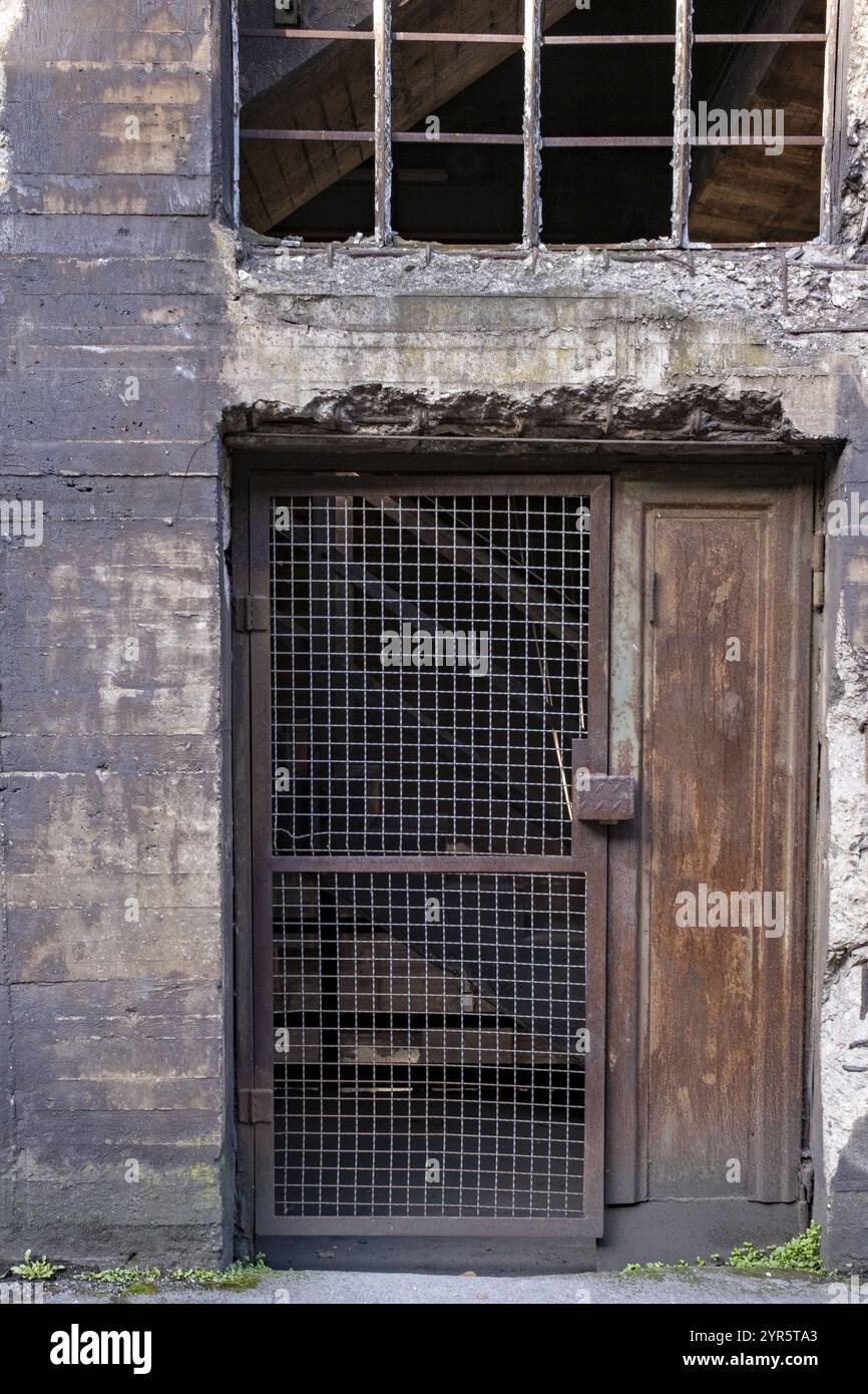 A rusted metal gate in a concrete wall, exhibiting industrial decay ...