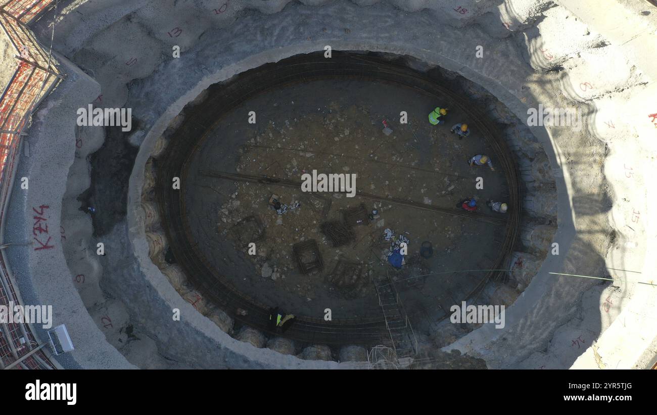 Aerial view of a construction site with a circular pit, visible workers ...