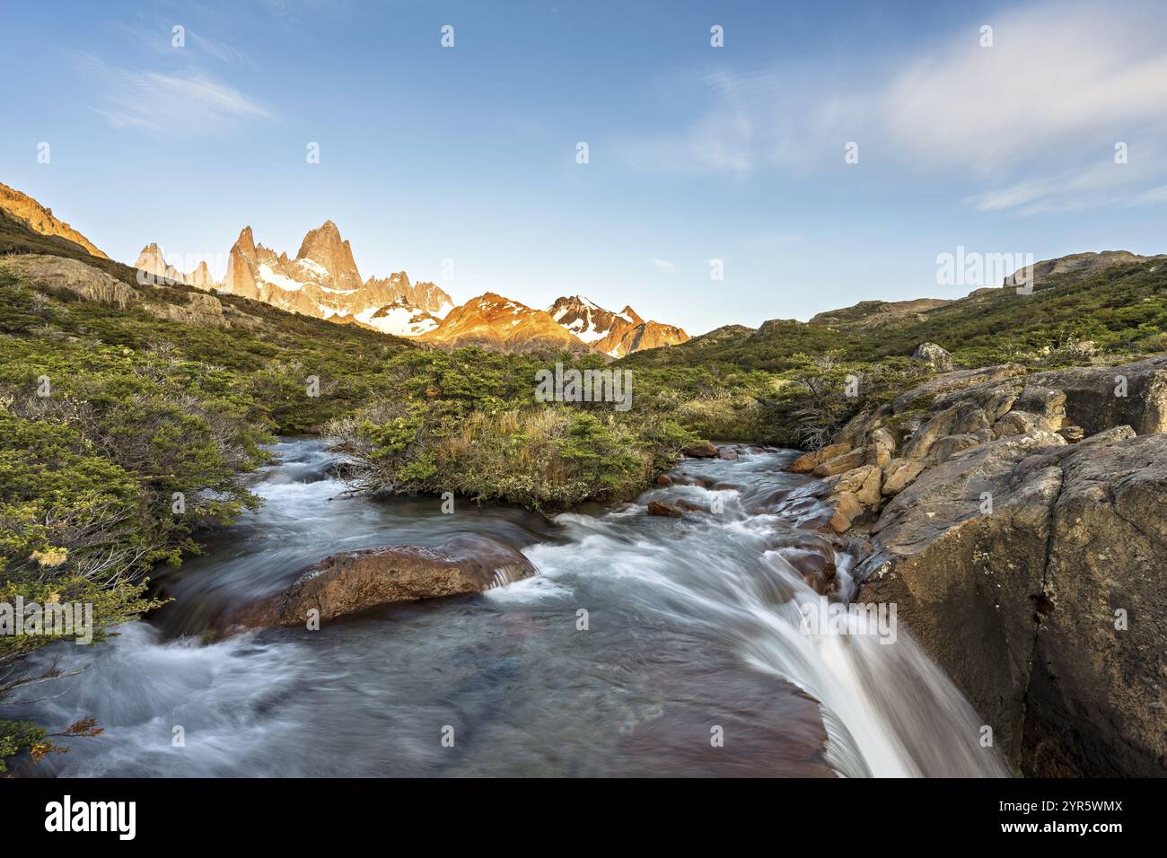 A waterfall with the Fitz Roy mountain illuminated by the morning sun ...