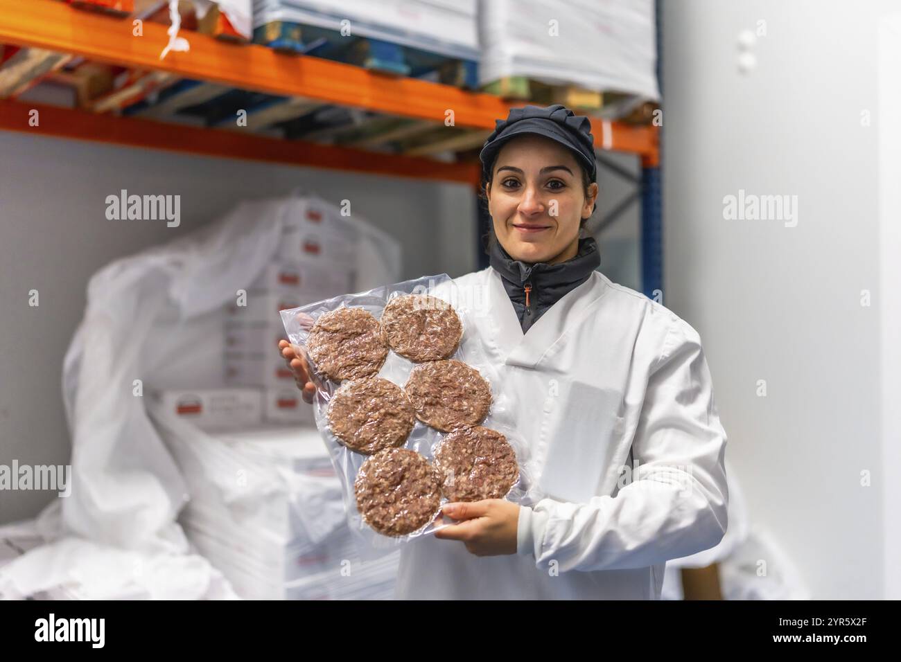 Woman worker in uniform and hygienic hat showing packed hamburgers in a ...