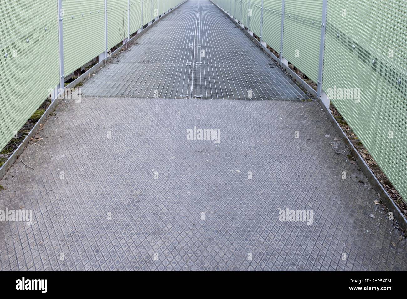 A long walkway with metal grid flooring and green rails, extending into ...