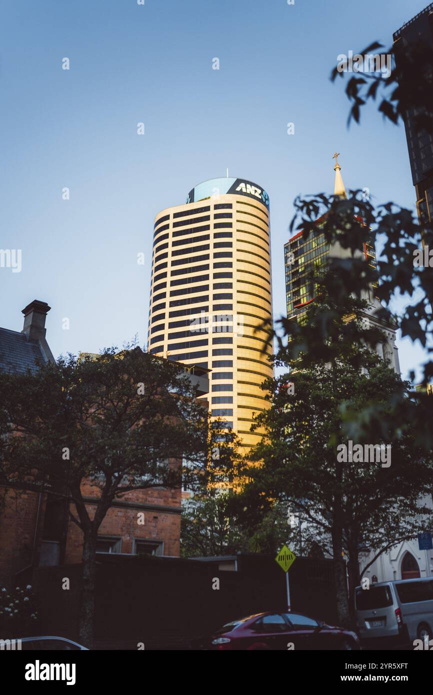 A round skyscraper with ANZ logo is surrounded by trees in the late ...