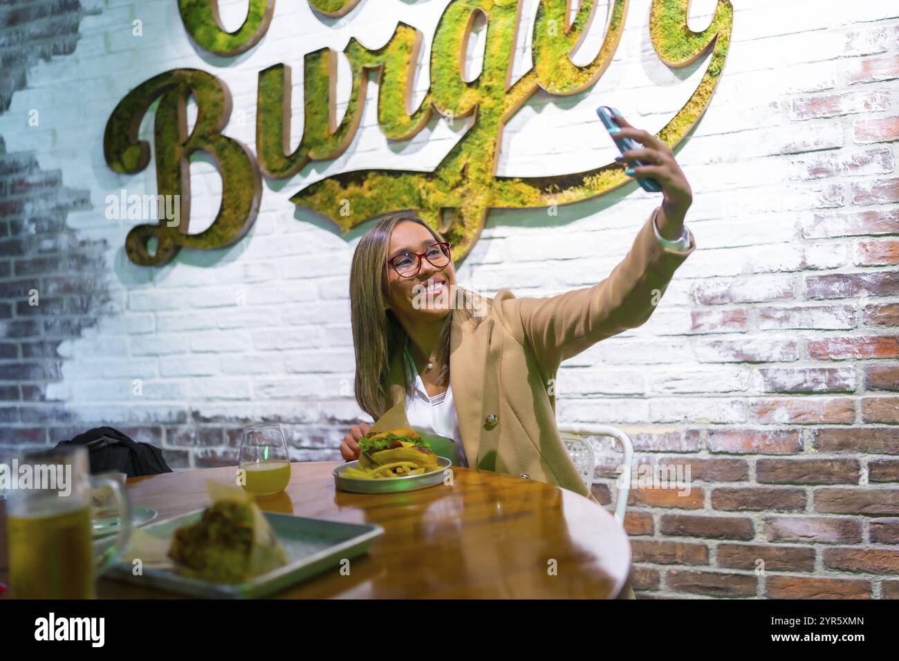 Happy latin blonde woman taking selfie while eating a tasty hamburger ...