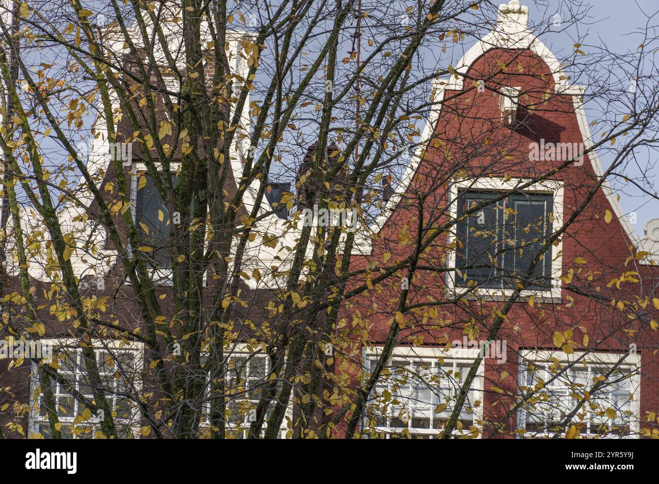 Brick building with gables partly covered by trees with autumn leaves ...