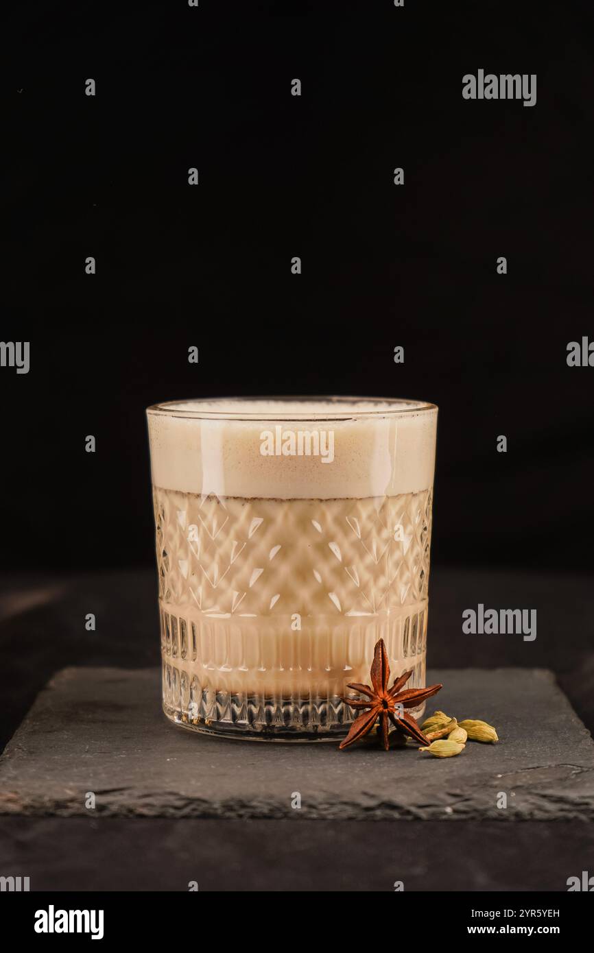 A glass cup of traditional Indian masala tea on a dark texture ...