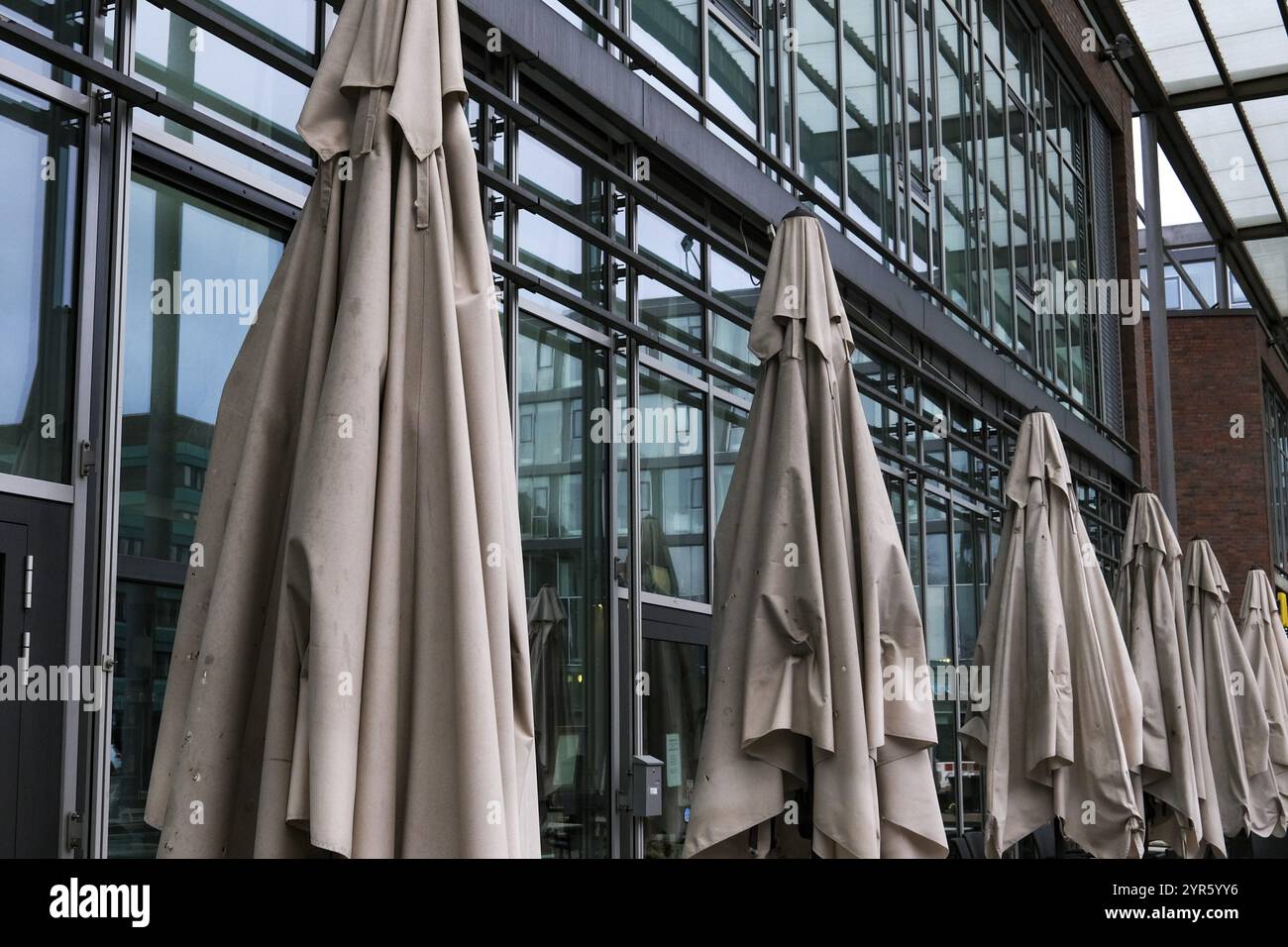 Row of closed beige umbrellas outside a modern glass building, creating ...