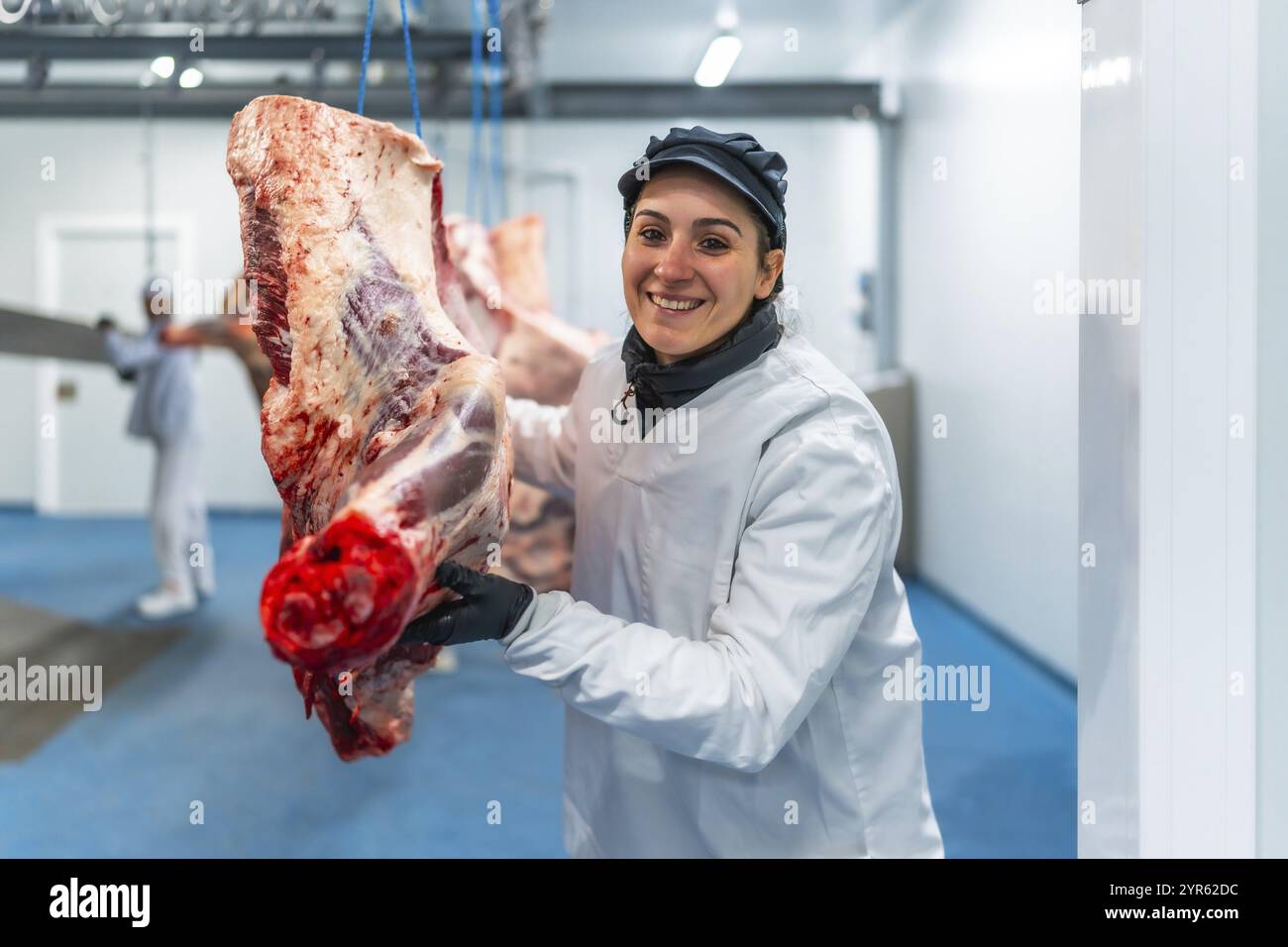 Happy female butcher carrying meat hanging in cold store of a ...