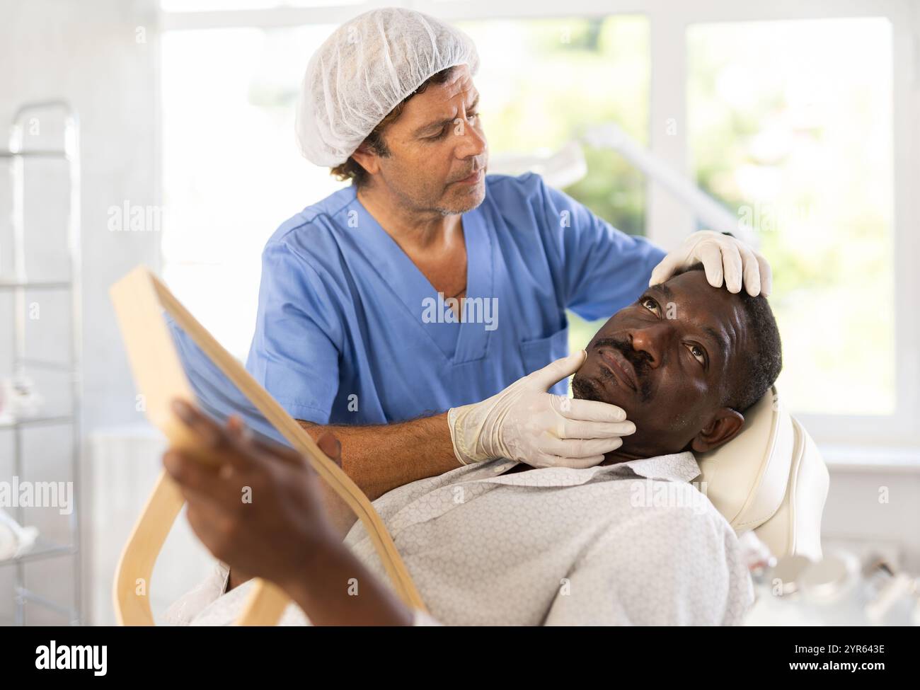 Male cosmetologist examines face of African man patient and consult on ...