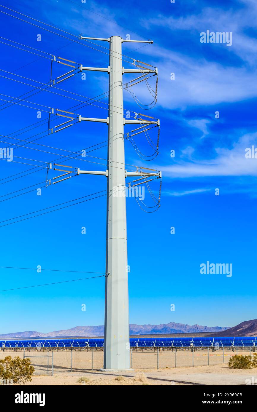 A tall power pole stands in a field with a clear blue sky above. The ...