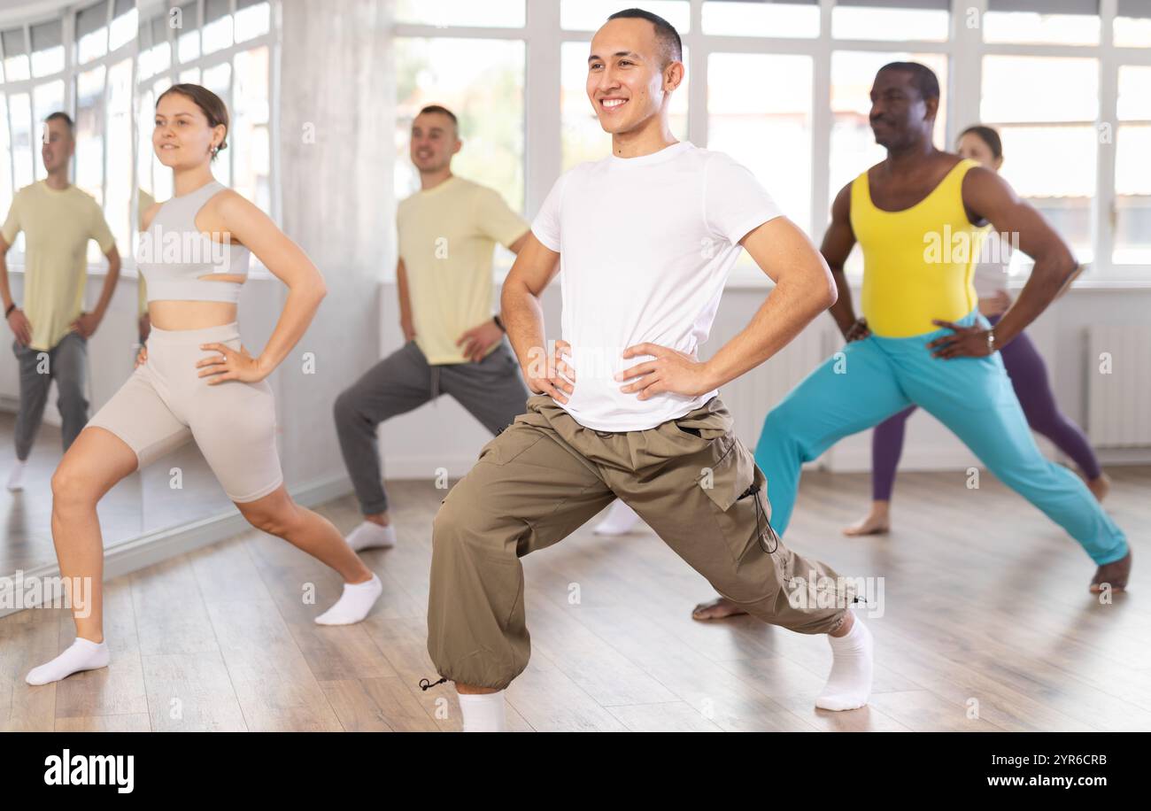 Cheerful Asian guy performing stretching exercises during dance class ...