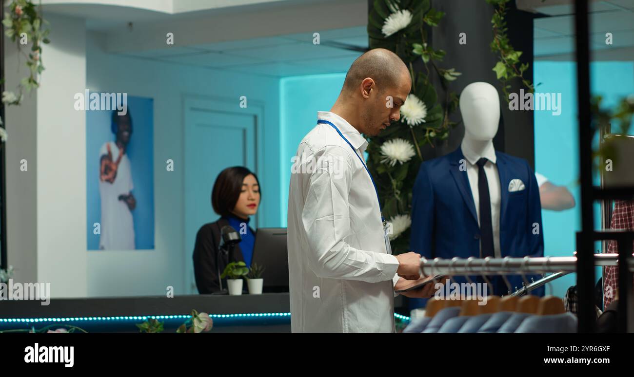 Male retail assistant organizing quality clothes on display in a store, enhancing the shopping ...