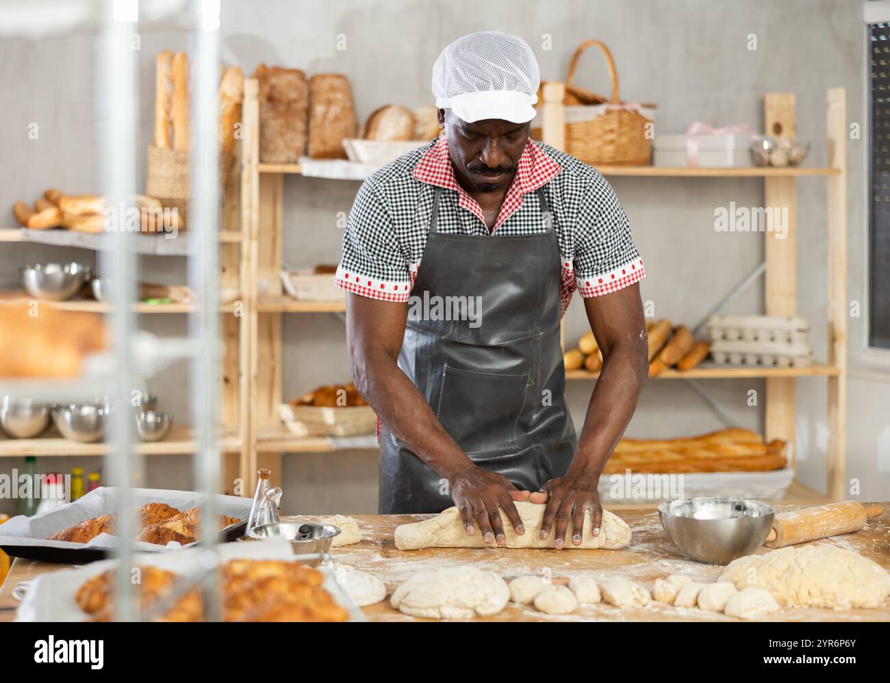 African American baker forming dough into long bread in bakery Stock ...