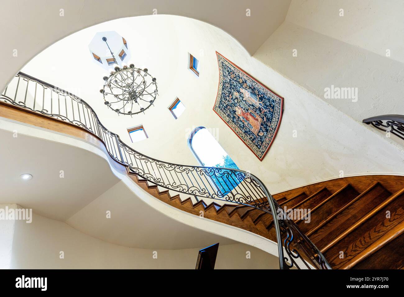Elegant spiral staircase with chandelier and wall tapestry in bright ...