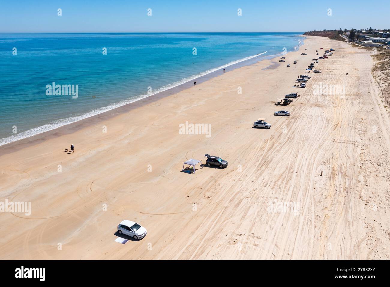 Aerial view of a line of four wheel drives on a wide sandy beach next a ...