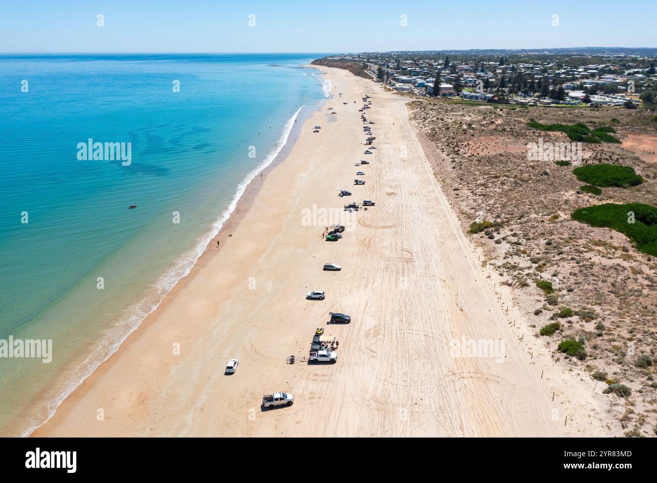 Aerial view of a line of four wheel drives on a wide sandy beach next a ...