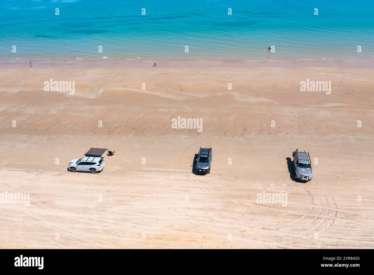 Aerial view of a line of four wheel drives on a wide sandy beach next a ...