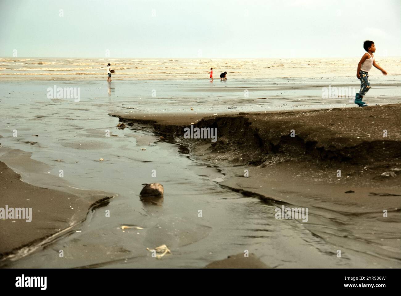 Children playing on the beach, close to a small stream estuary at Pakis ...