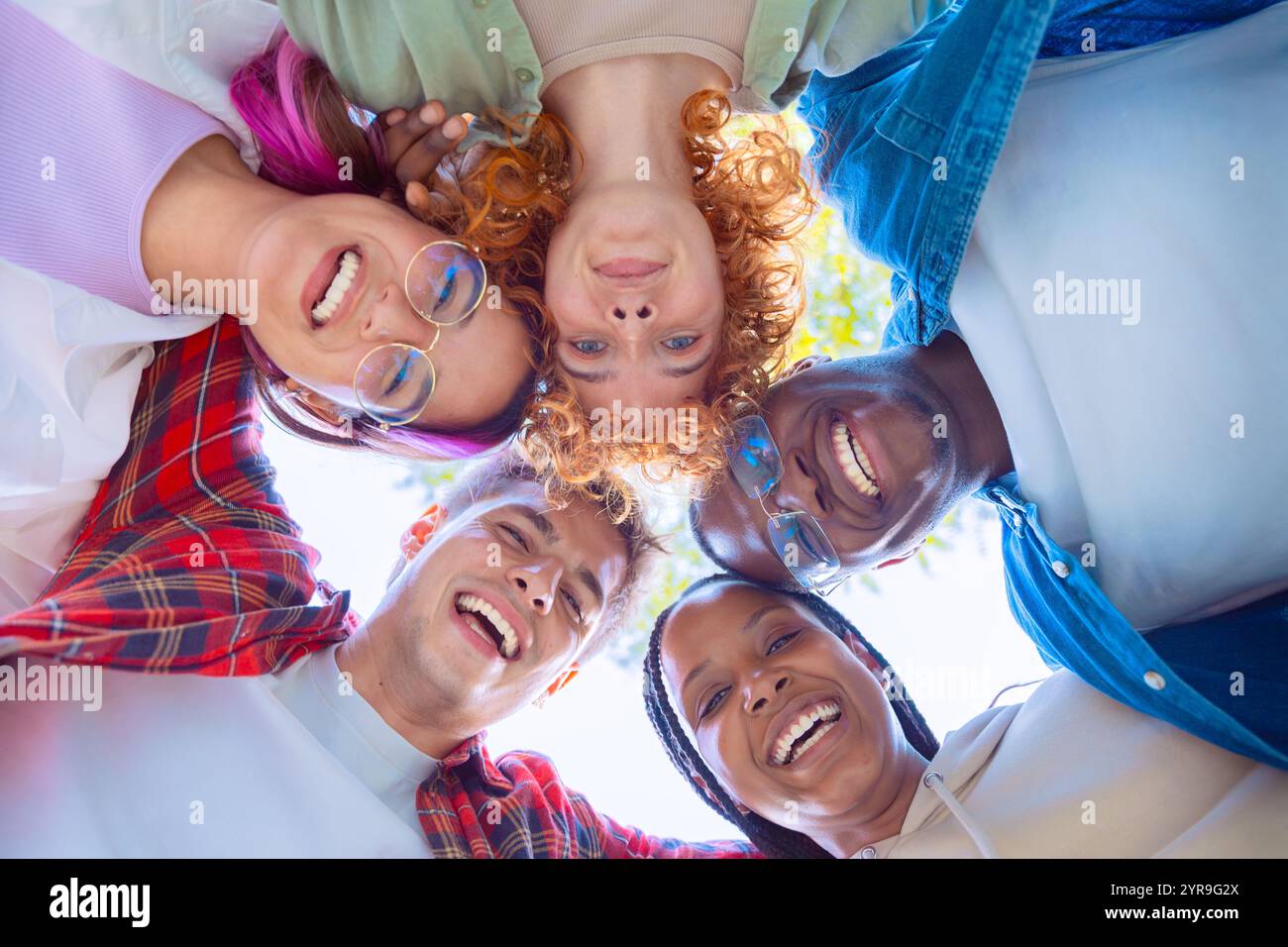 Group of diverse young people smiling and looking down in a circle ...