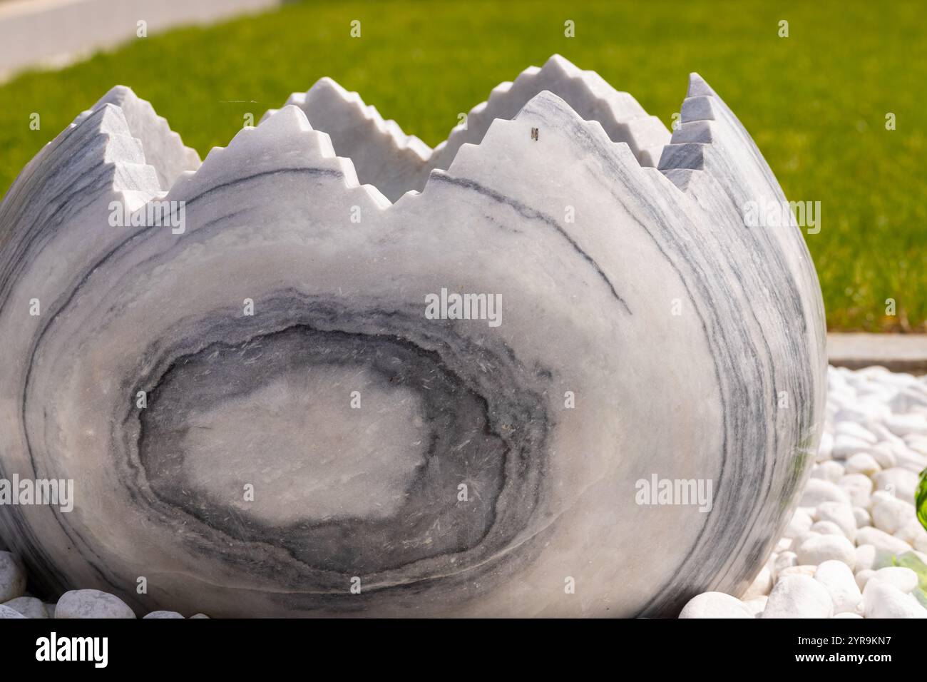 Large broken marble egg as a water fountain in a stone bed. High ...