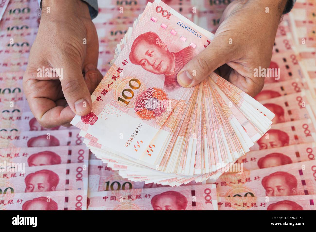 Hand Holding Stack of 100 Yuan Notes on table. Translate alphabet Yibai ...