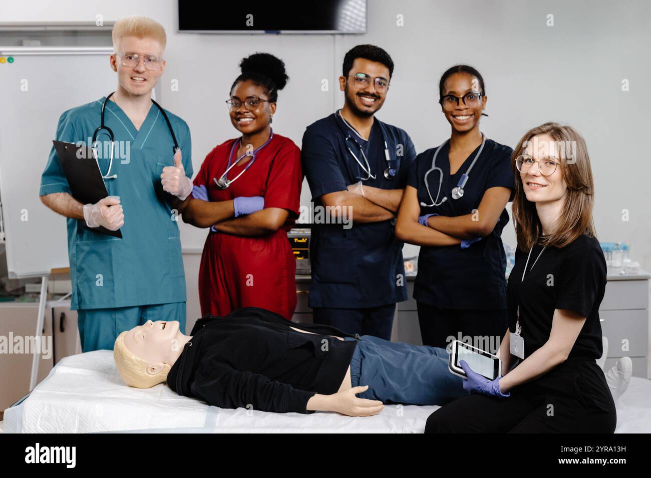 A group of doctors in medical scrubs standing around a mannequin lying ...