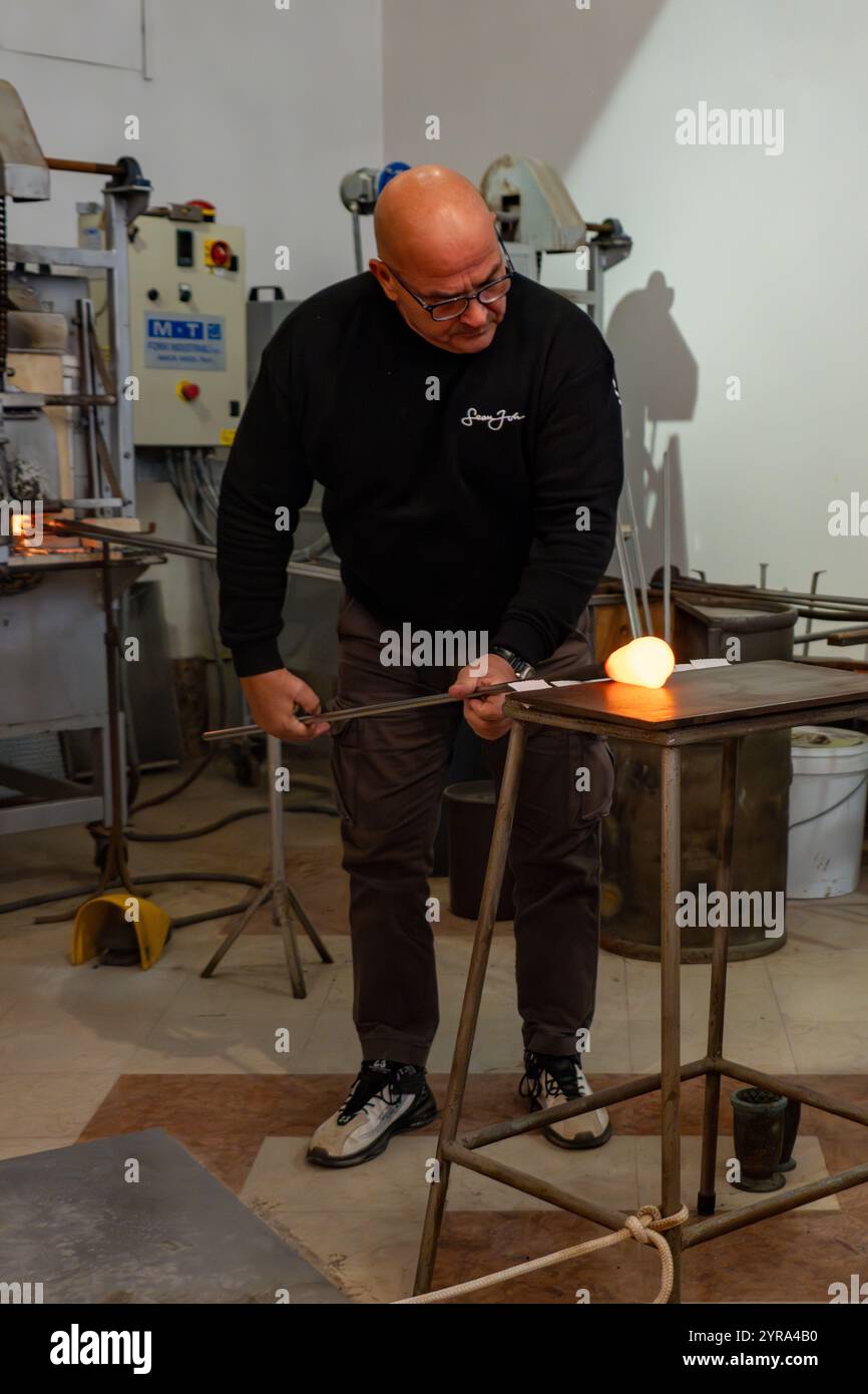 The glassblower rolls the molten gather on a marver in a glassblowing ...